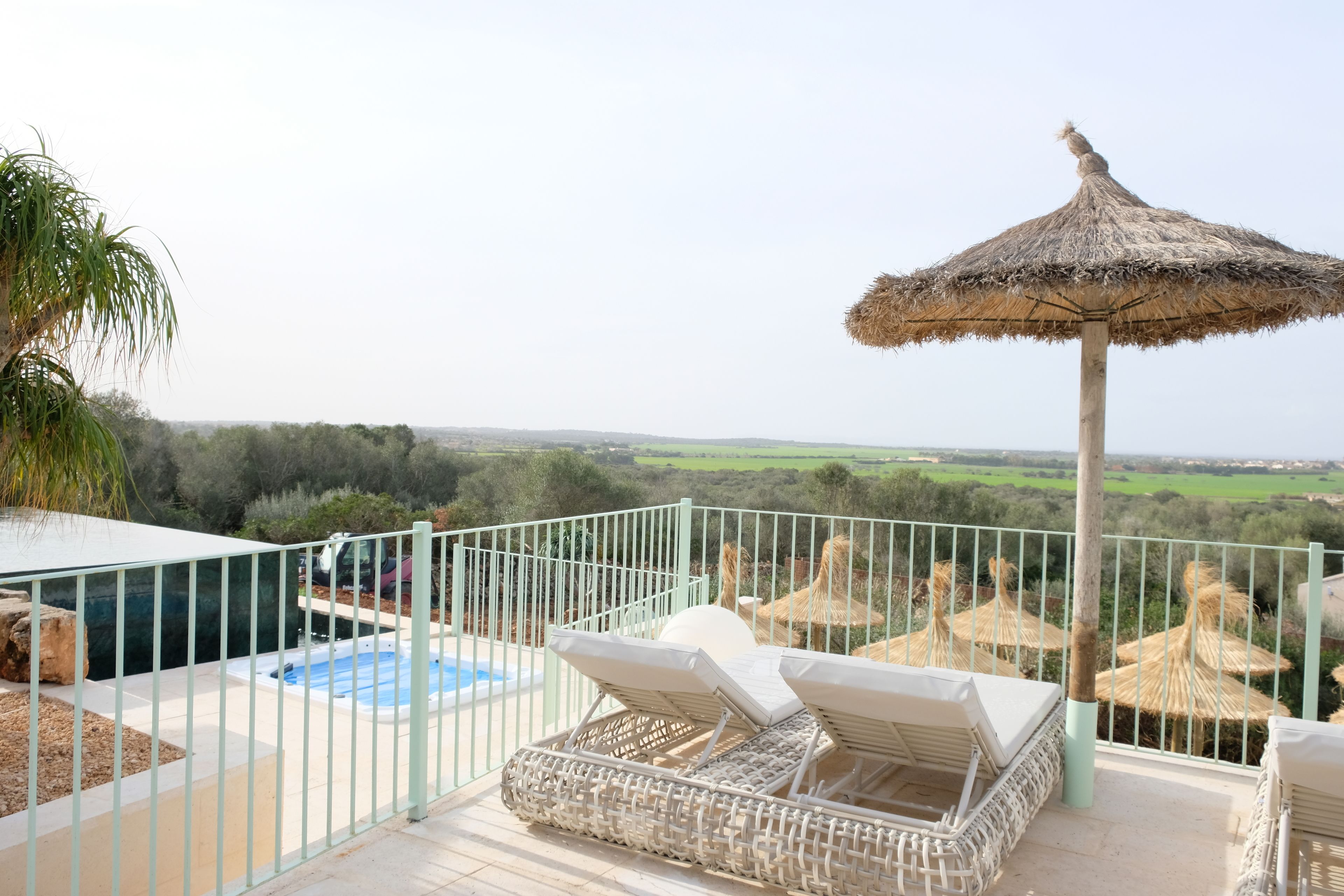 Área de piscina com espreguiçadeiras e um guarda-sol de palha, com vista para uma paisagem deslumbrante.