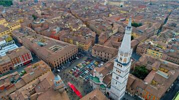 Vista aérea de uma área urbana densamente povoada, com edifícios históricos, uma torre imponente e uma praça central com carros estacionados.