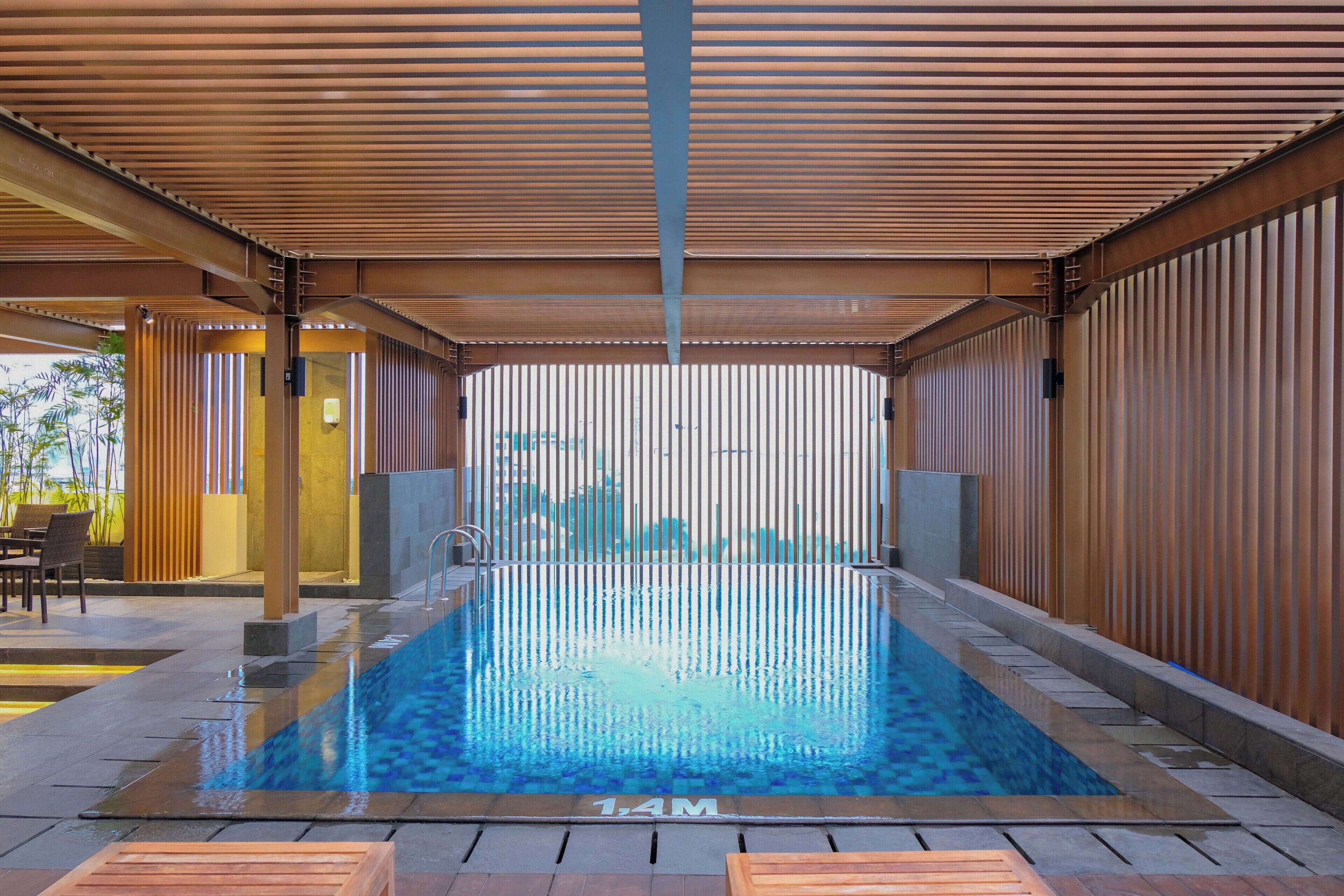 Piscina com 14 metros de comprimento, cercada por painéis de madeira e área coberta com assentos.
