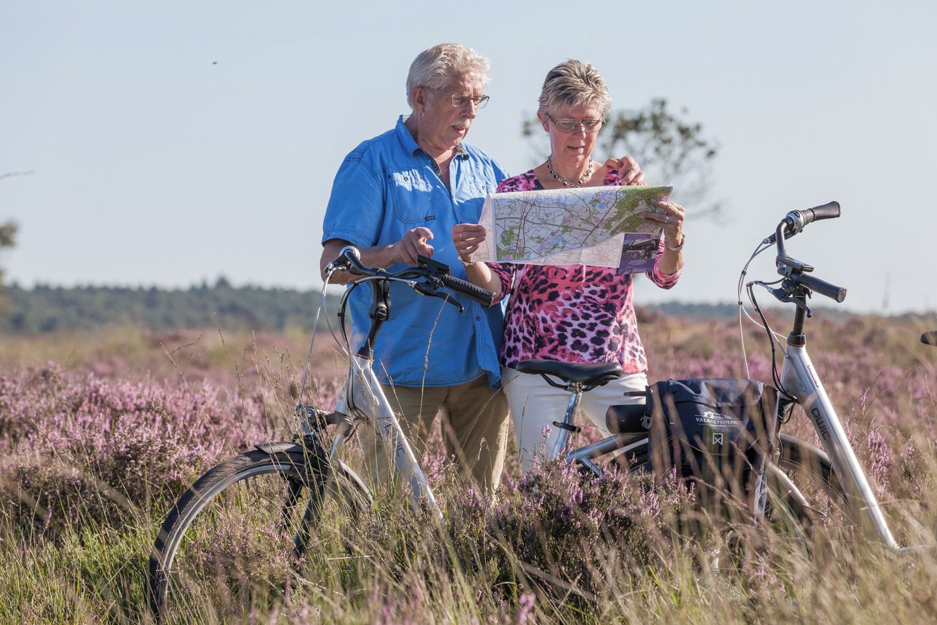 Duas pessoas em um campo com bicicletas, uma segurando um mapa.