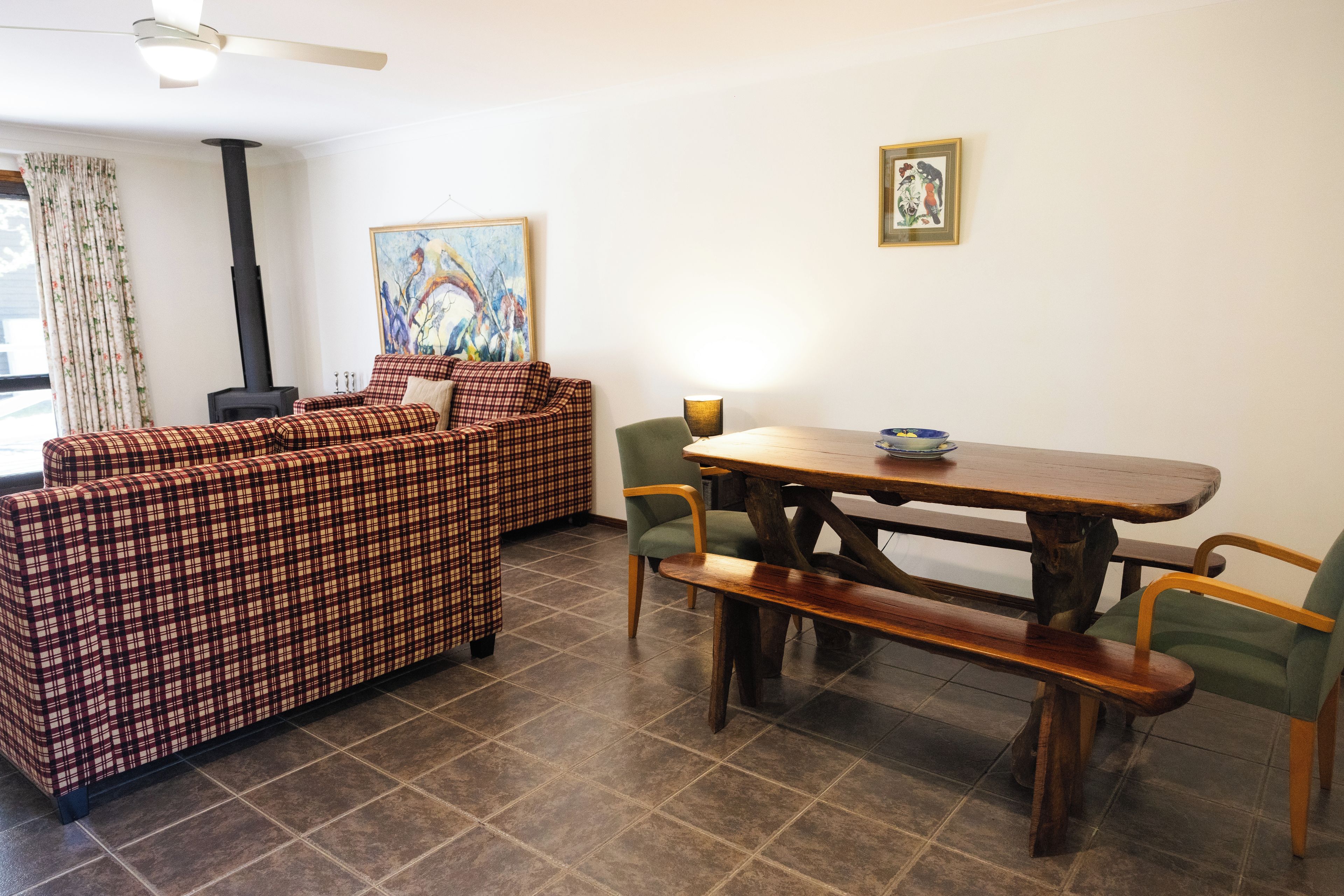 Uma sala de estar com sofá, mesa de jantar com cadeiras, quadro na parede e lareira.