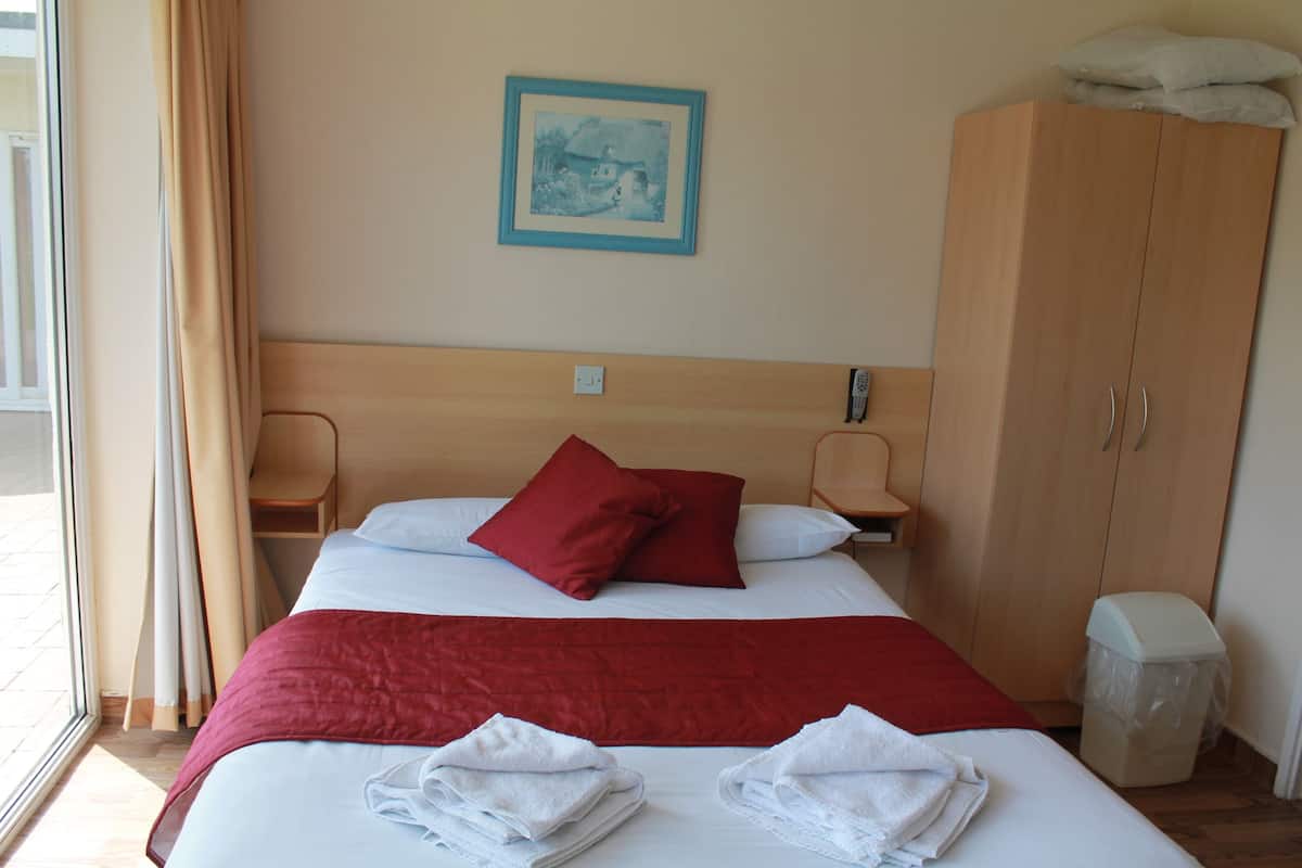 Quarto de hotel com cama, travesseiro vermelho, cobertor branco, guarda-roupa de madeira e uma imagem na parede.