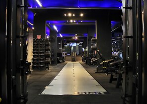 Academia com equipamentos de musculação, linha de partida e uma tela de televisão ao fundo.