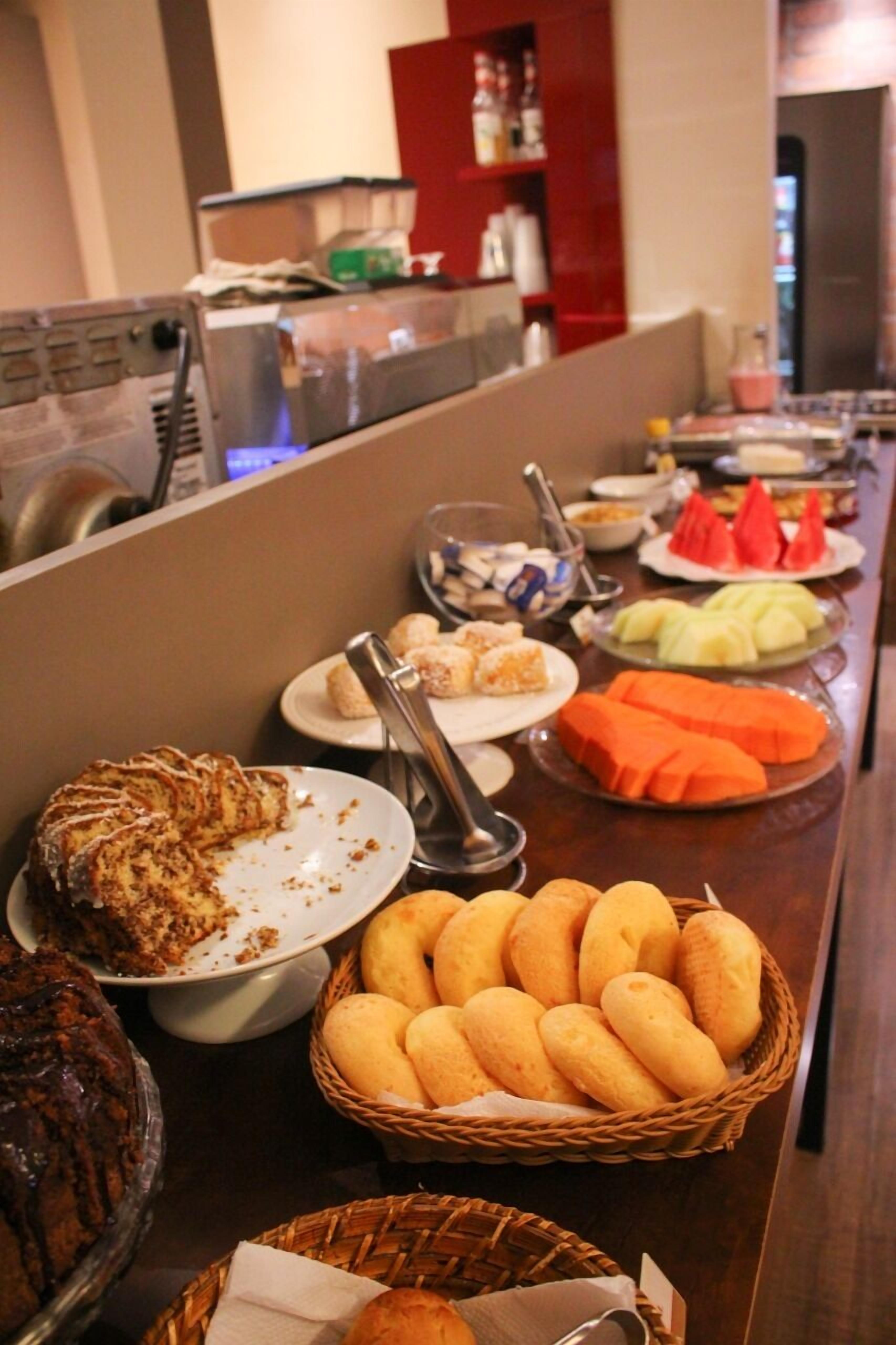 Buffet com diversos alimentos, incluindo pão, frutas e sobremesas.