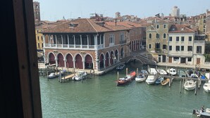 Vista de um canal com barcos atracados, uma ponte e edifícios históricos com janelas em arco.