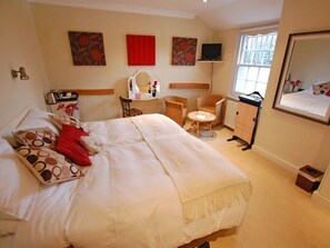 Quarto de hotel com uma cama grande, um espaço de estar com uma cadeira e uma mesa pequena, uma TV fixada na parede e uma janela com vista para o exterior.