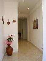 Um corredor com um vaso de flores, um quadro na parede e uma porta no final.