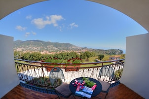 Uma varanda com vista para uma paisagem montanhosa, uma mesa com uma revista e duas cadeiras.