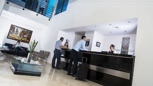 Uma área de recepção de hotel com design moderno, incluindo um balcão de atendimento, espaço para sentar e uma escada que leva a um andar superior.