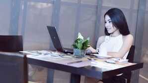 Uma pessoa sentada à mesa com um laptop, papéis e uma xícara.