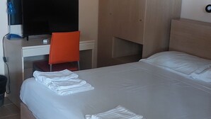 Quarto de hotel com uma cama, uma secretária com um computador e uma cadeira.
