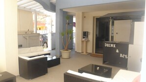 Uma área de estar moderna com um sofá, uma mesa de centro e uma planta em vaso. Há uma placa com a inscrição "DRINK & BEE".