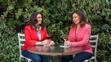 Duas mulheres sentadas numa mesa redonda ao ar livre, com um fundo verde exuberante.