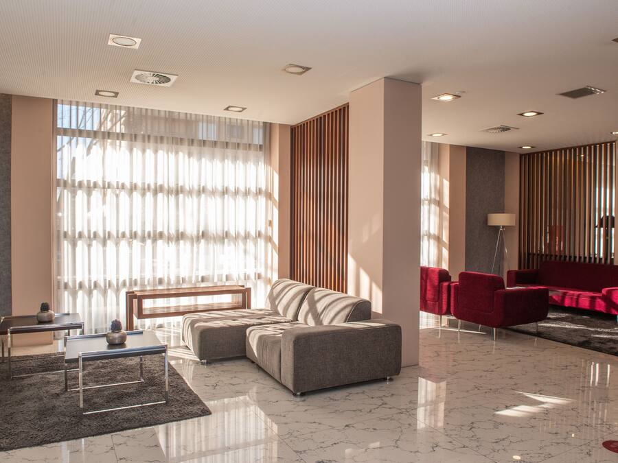 Um hall de hotel moderno com um sofá em seção, uma mesa pequena e cadeiras vermelhas.