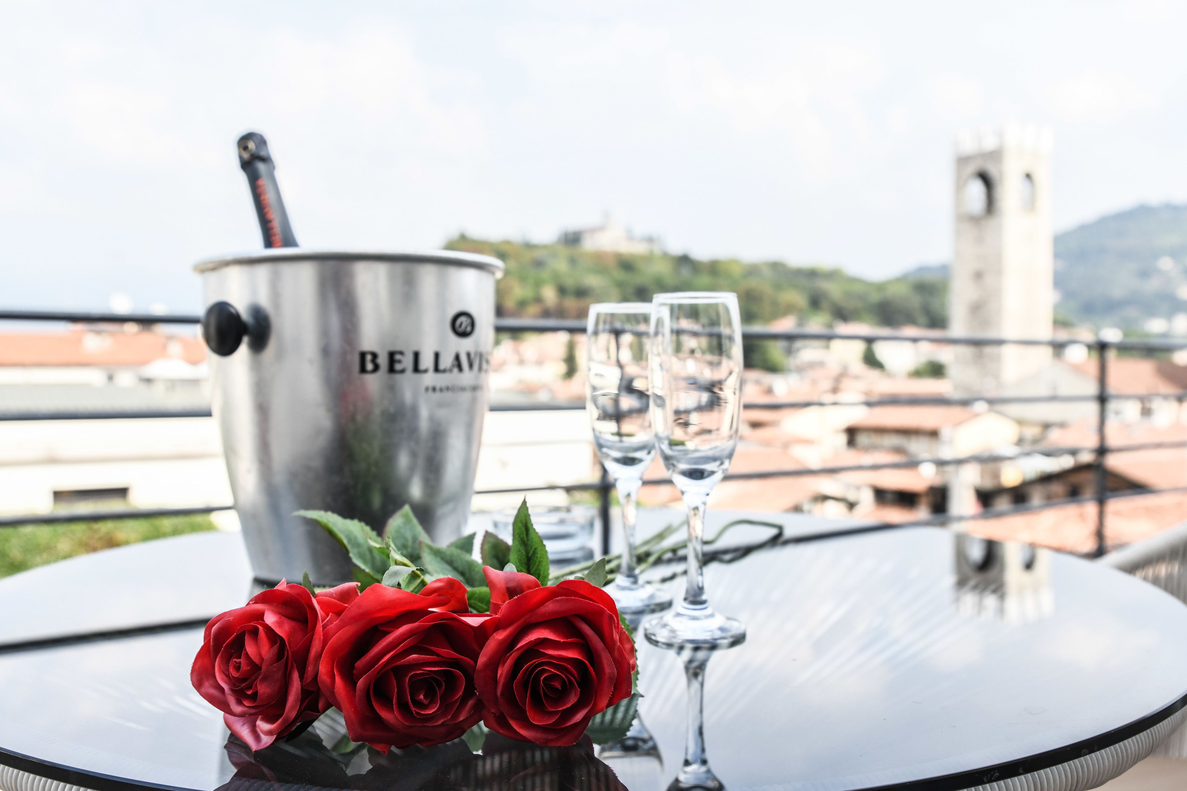 Uma mesa com balde de champanhe, duas taças de vinho e três rosas vermelhas.