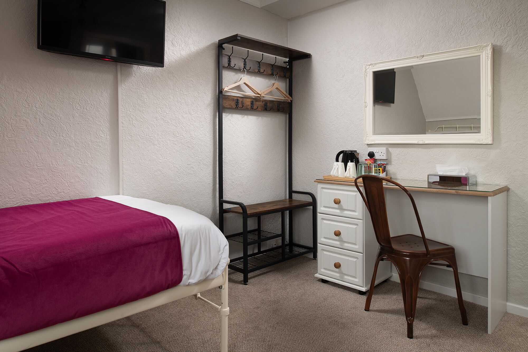 Quarto com cama, escrivaninha com cadeira, televisão e cabideiro.