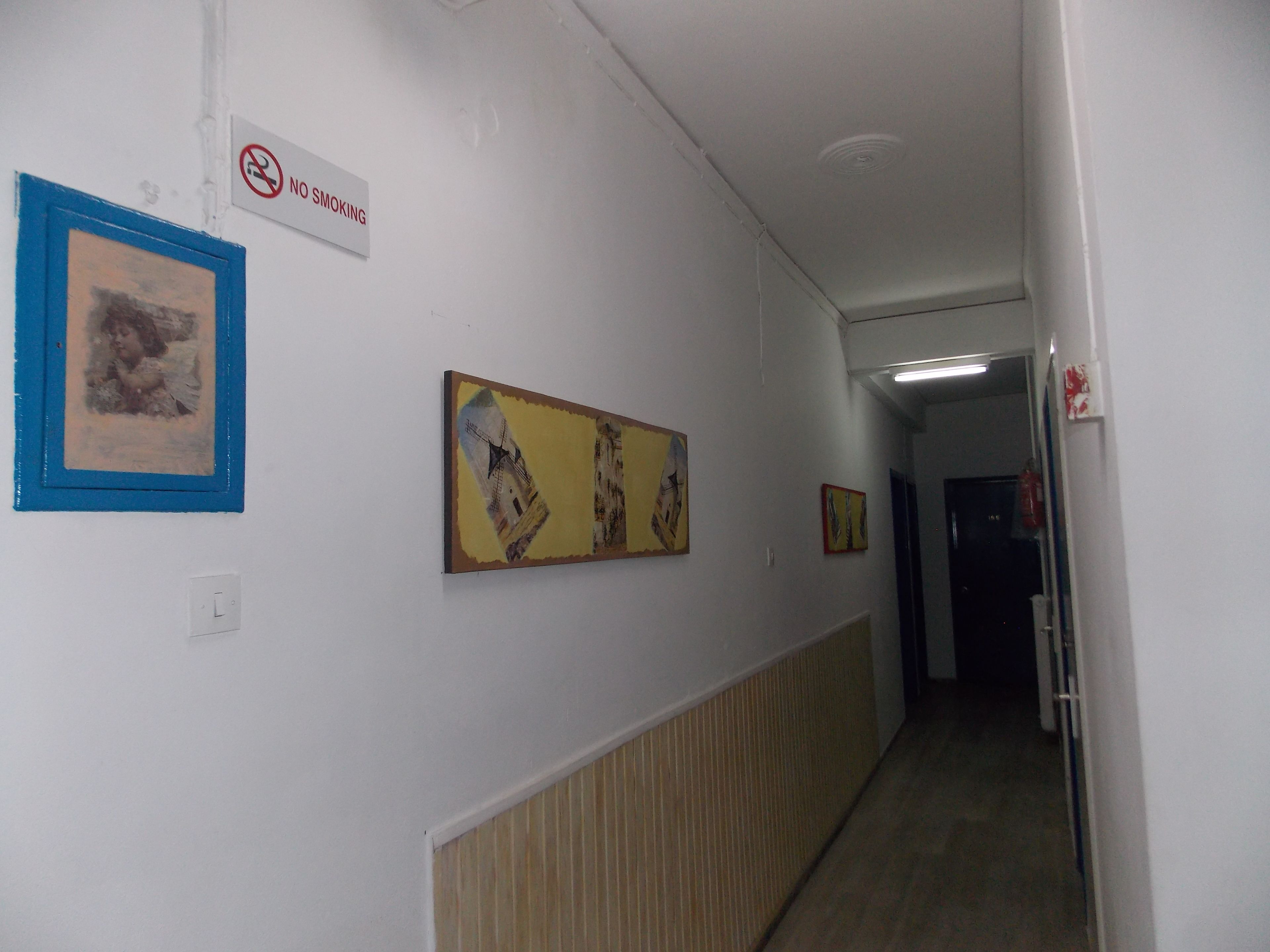 Um corredor com obras de arte nas paredes, um aviso de proibido fumar e uma porta no final.