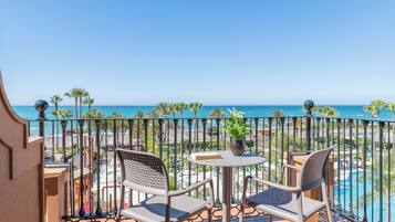 Varanda com duas cadeiras e uma mesa pequena, com vista para uma piscina e uma praia.