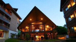 Um hotel moderno com uma estrutura triangular marcante no telhado, grandes janelas e área externa bem cuidada com acesso circular.