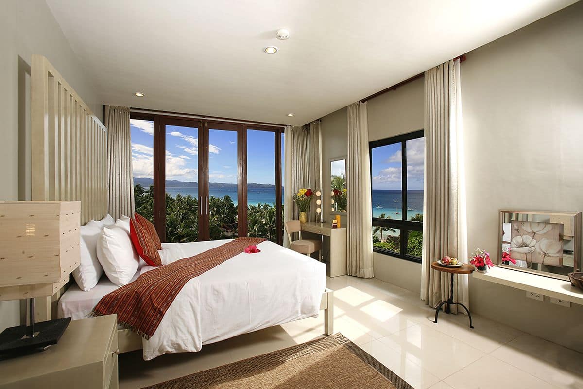 Quarto de hotel moderno com uma cama grande, uma escrivaninha e vista para o oceano.