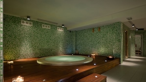 Uma área de spa com uma banheira de madeira, paredes com mosaico verde e iluminação embutida.