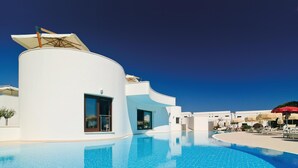 Um resort moderno com uma grande piscina infinita, arquitetura branca e guarda-sóis vermelhos.