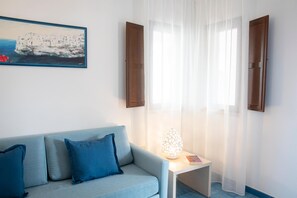 Um quarto com um sofá azul claro, uma mesa pequena com uma luminária decorativa, cortinas finas e um quadro na parede.