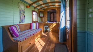 Interior acolhedor de uma cabana com um banco de madeira, um banquinho pequeno e uma janela com persianas de madeira.