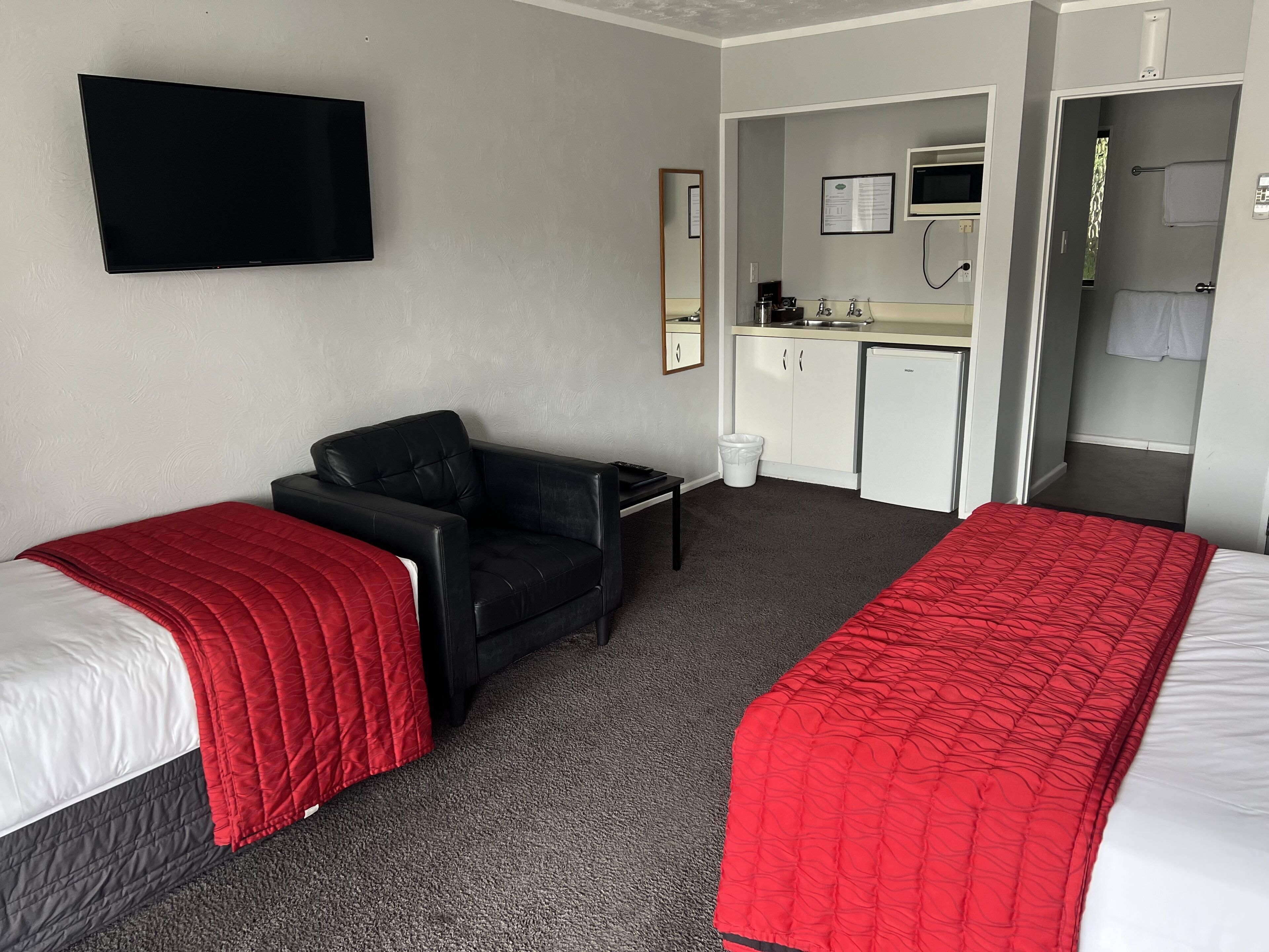Quarto de hotel com duas camas, televisão, cozinha compacta e banheiro.