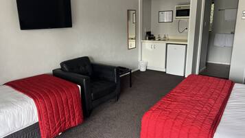 Quarto de hotel com duas camas, televisão, cozinha compacta e banheiro.
