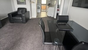 Um espaço compacto com cozinha americana, área de refeições com mesa de vidro e espaço de estar com poltrona de couro preta.