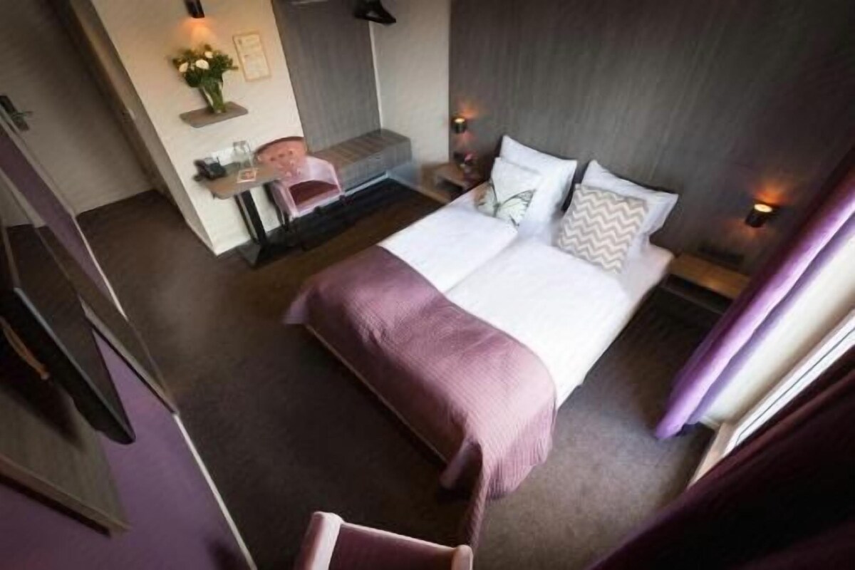 Quarto de hotel com cama, área de estar e uma mesinha com um vaso de flores.