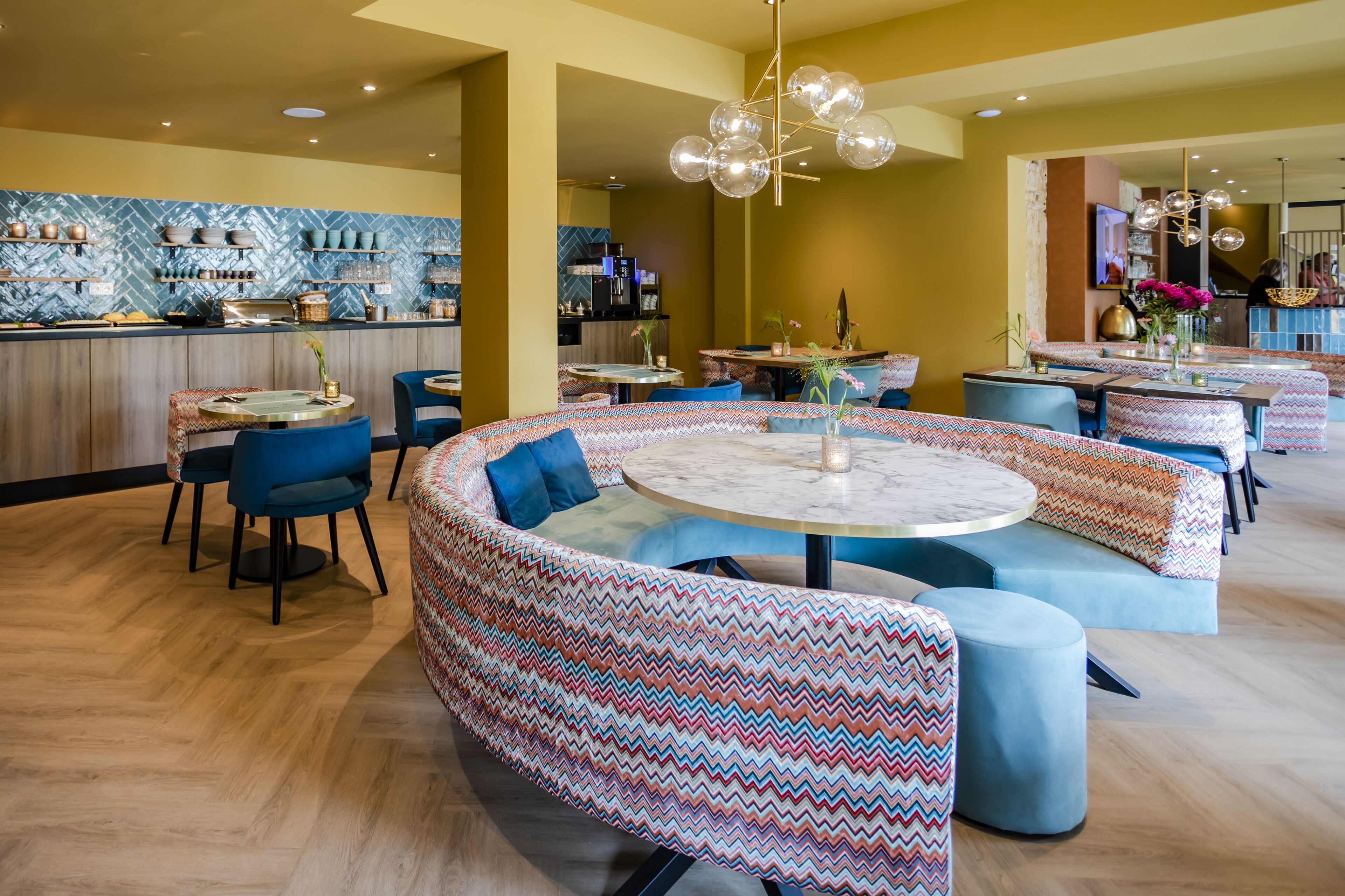 Um restaurante moderno com mesas redondas, assentos estofados em azul e uma luminária decorativa no teto.