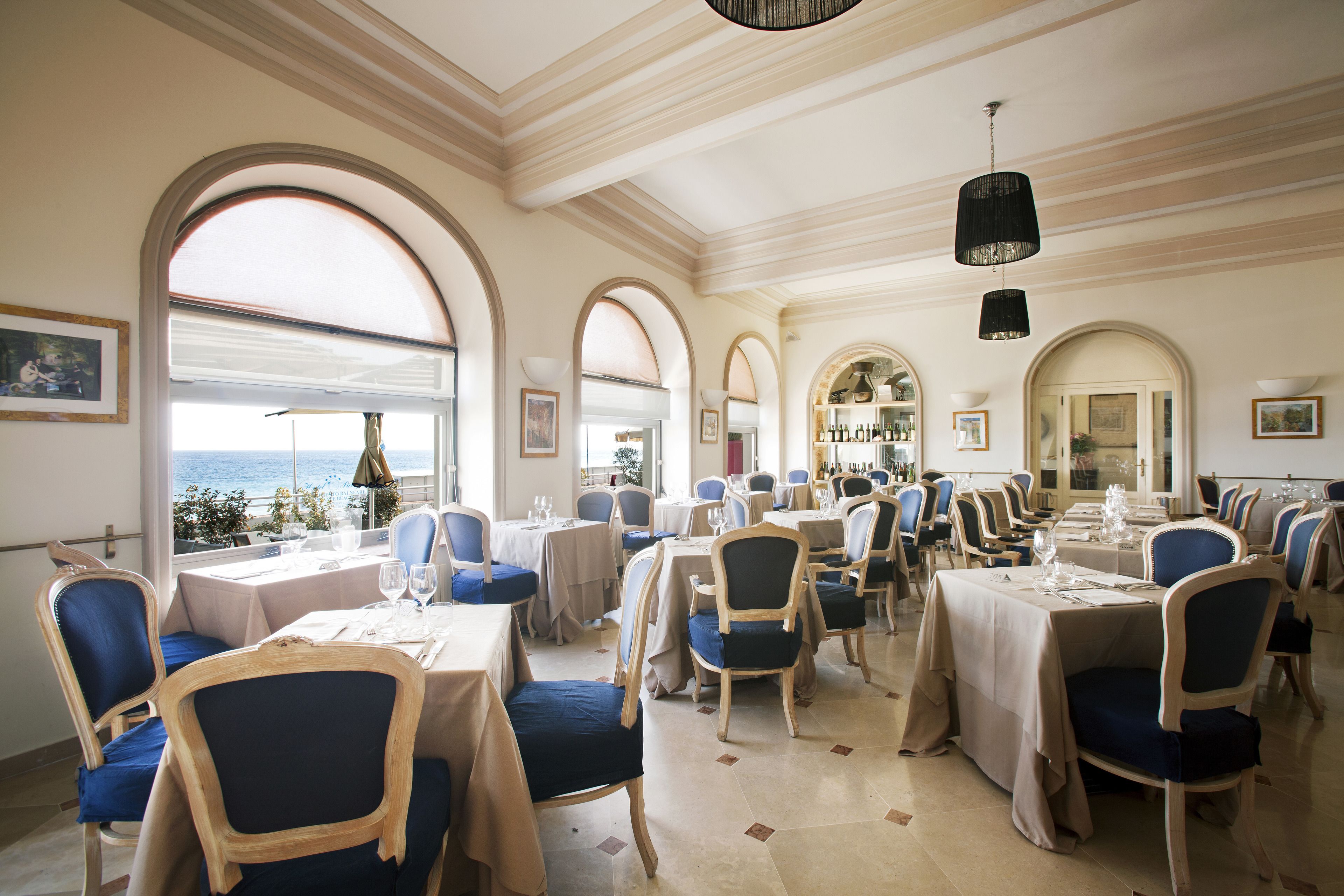 Um restaurante com várias mesas e cadeiras, janelas amplas com vista e decoração clássica.