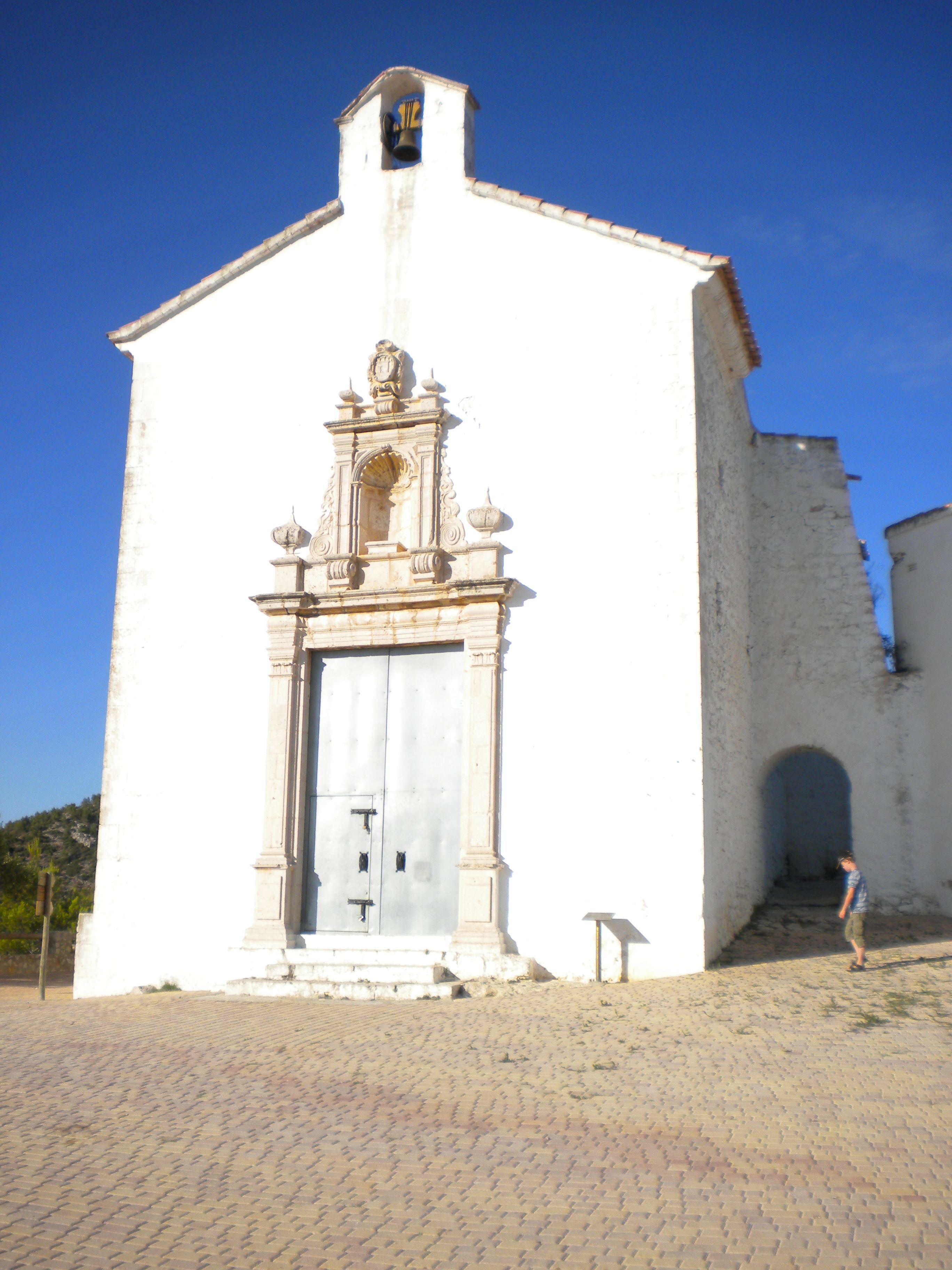 Uma igreja branca com uma torre de sino e uma porta grande.