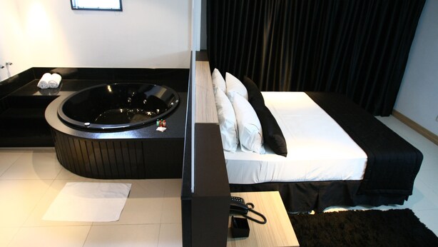 Quarto de hotel moderno com uma cama grande, cabeceira preta, esquema de cores preto e branco, banheira preta e uma janela pequena.