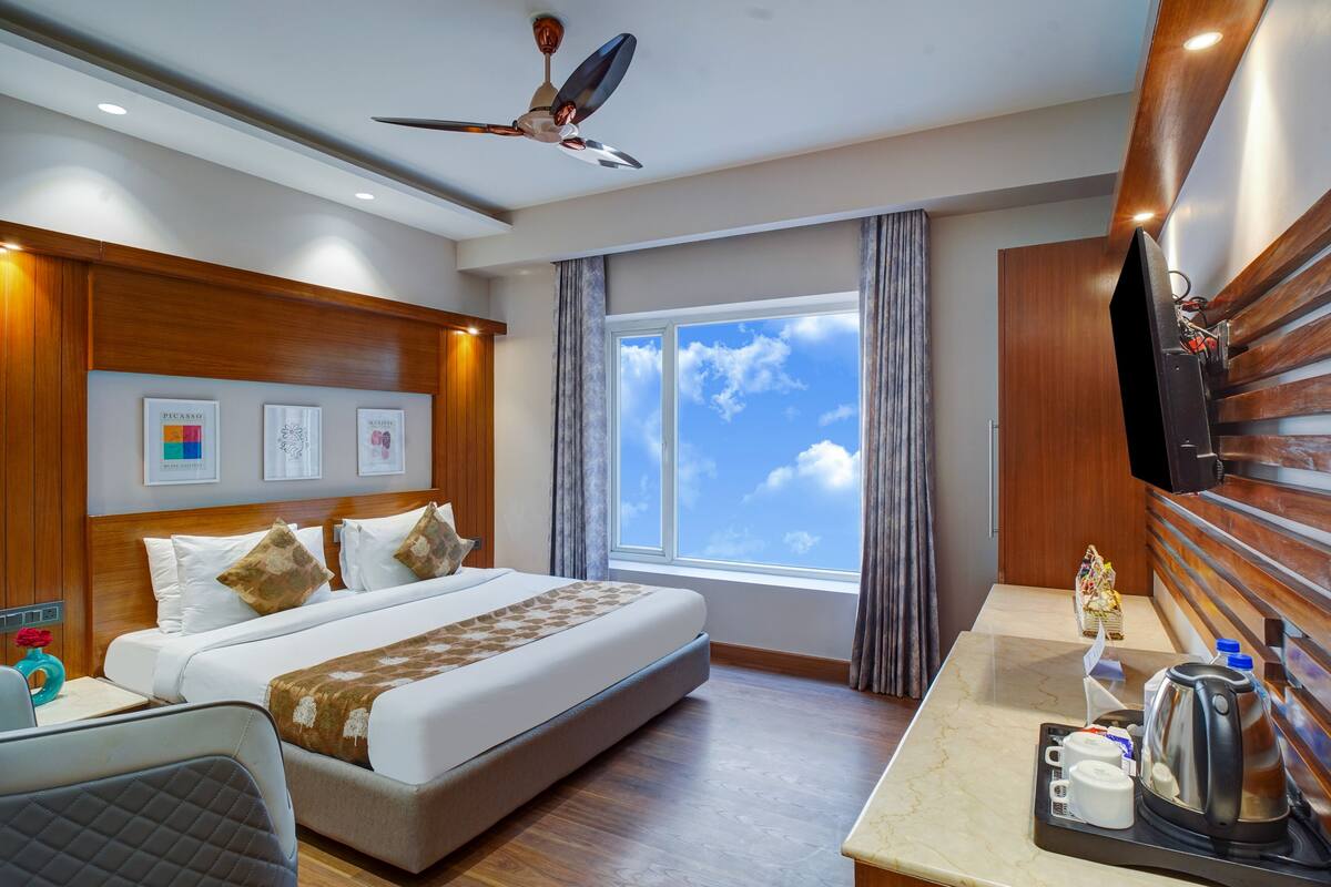 Quarto de hotel com cama, secretária com máquina de café, televisão e janela com cortinas.