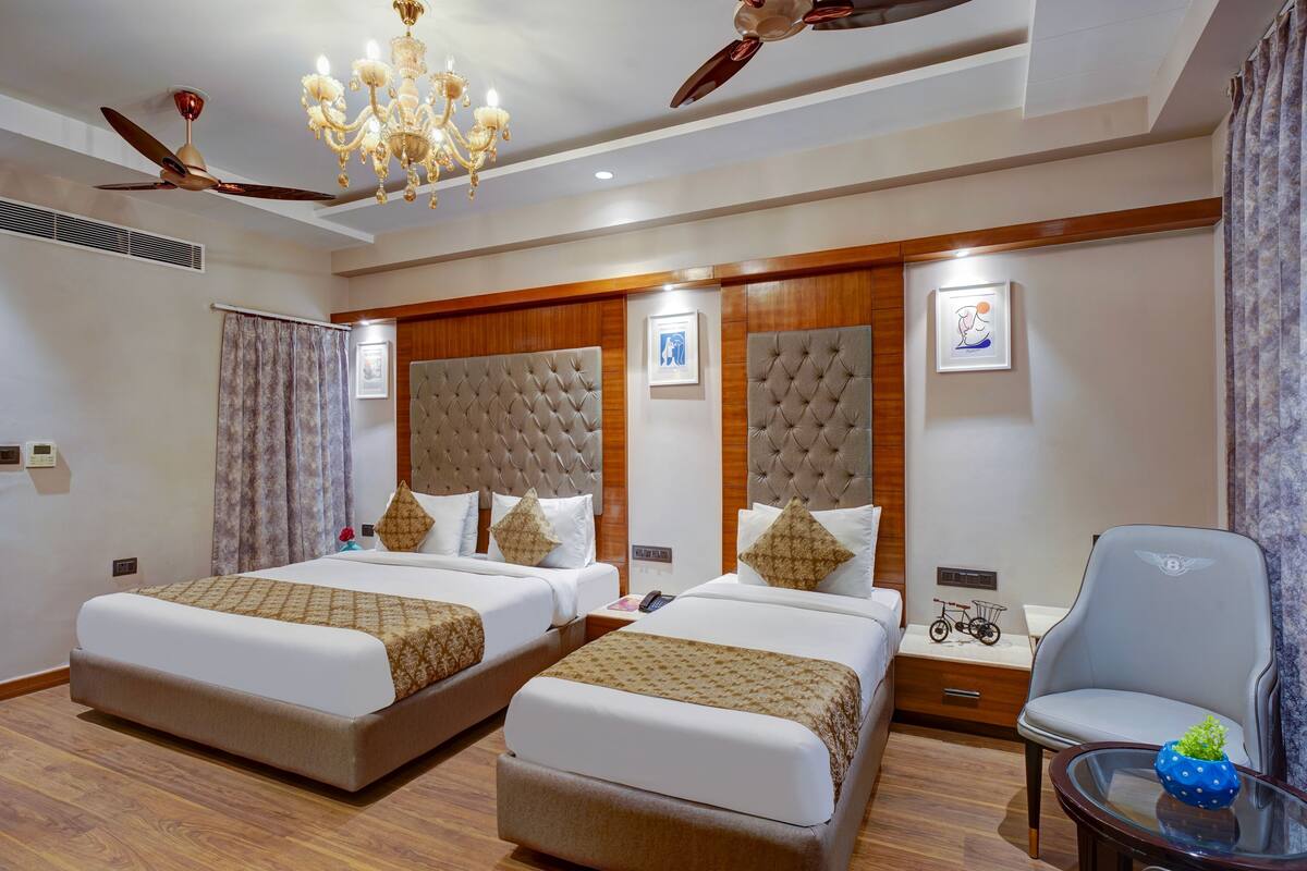 Quarto de hotel com duas camas, um candelabro, ventiladores de teto e uma pequena mesa com uma cadeira.