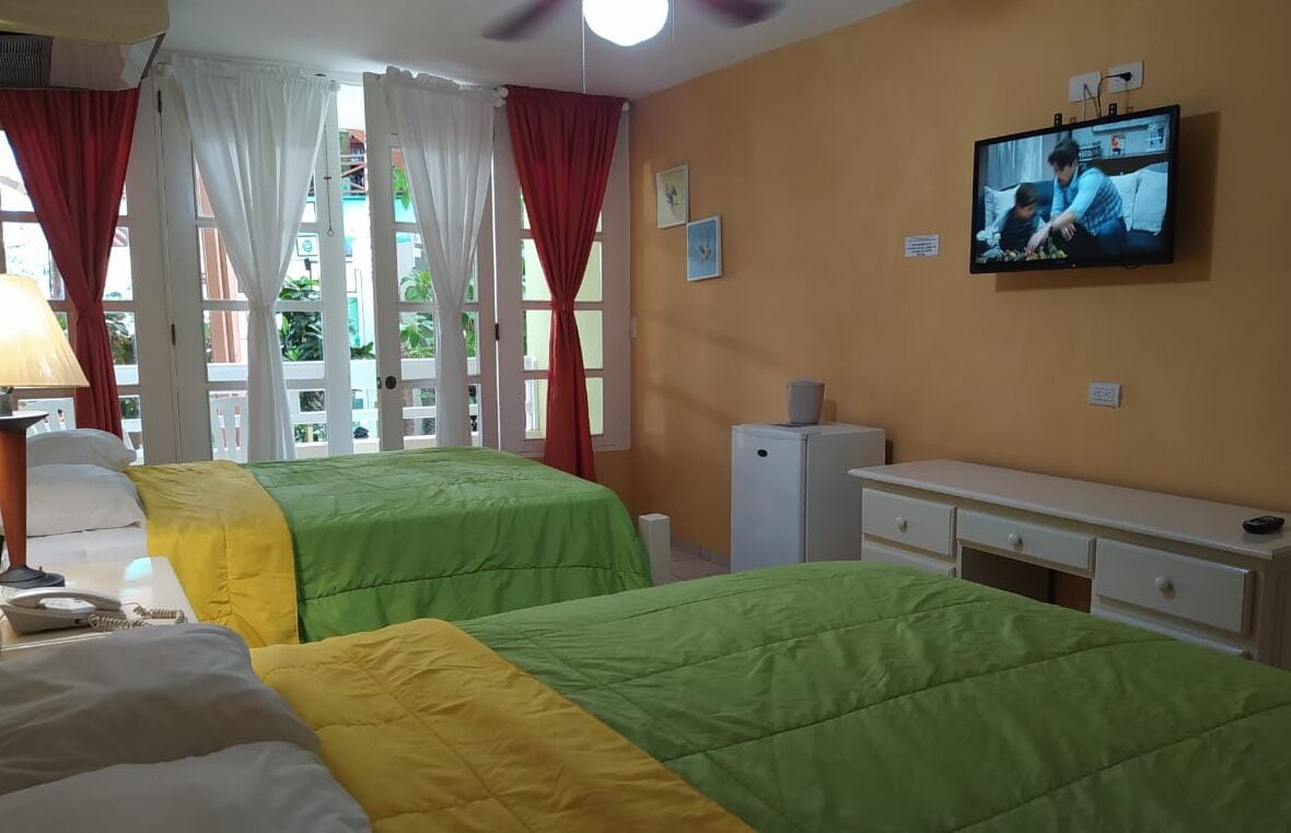 Quarto de hotel com duas camas, televisão, escrivaninha e janela com cortinas.