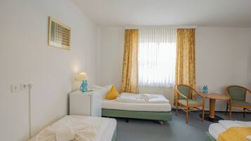 Quarto de hotel com cama, secretária, cadeira e janela com cortinas.