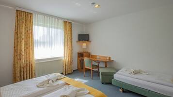 Quarto de hotel com duas camas, uma mesa, uma cadeira, televisão e janela com cortinas.