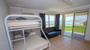 Quarto com uma cama de solteiro, um sofá e uma porta de correr para uma varanda com vista para a praia.