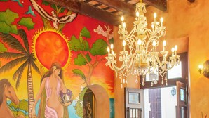 Restaurante com um mural, mesas de madeira e um candelabro.