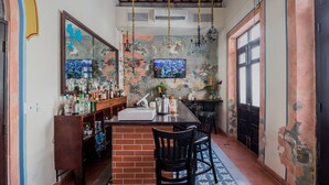 Uma área de bar com balcão de tijolos, cadeiras pretas e uma tela de televisão.