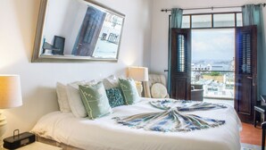 Quarto de hotel com uma cama grande, vista da cidade pela janela e um espelho na parede.