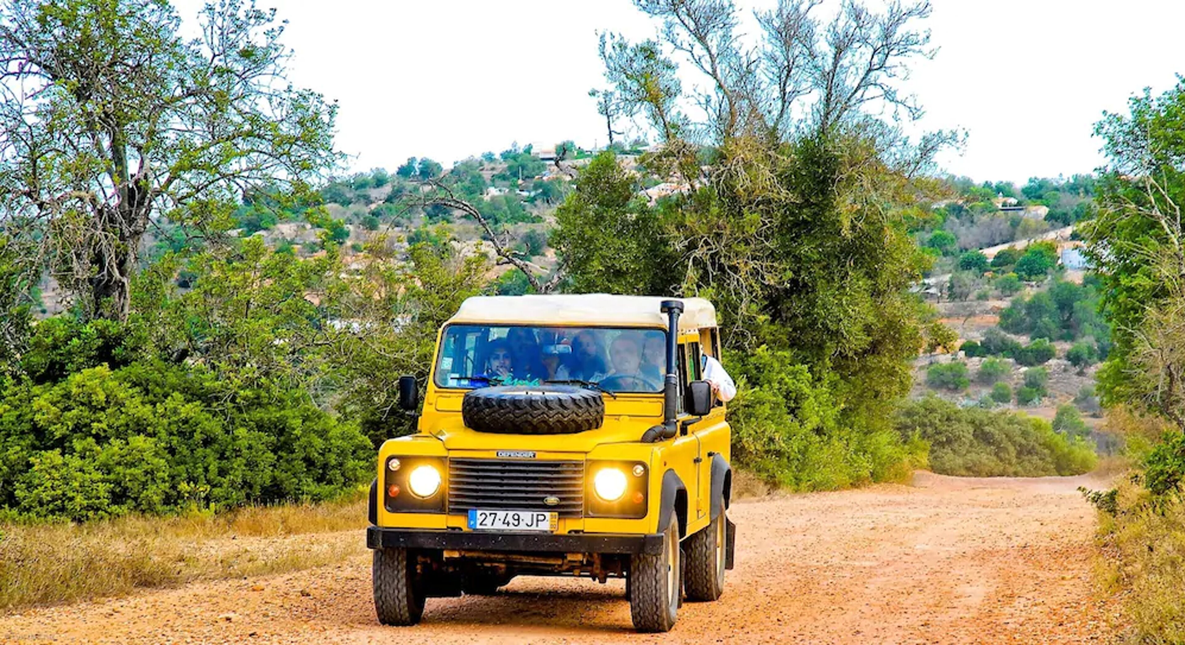 Um veículo todo-terreno amarelo numa estrada de terra, rodeado por vegetação.