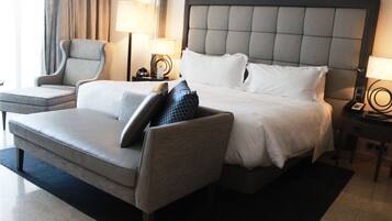 Quarto de hotel com uma cama grande, um sofá, uma poltrona e duas mesas de cabeceira com luminárias.