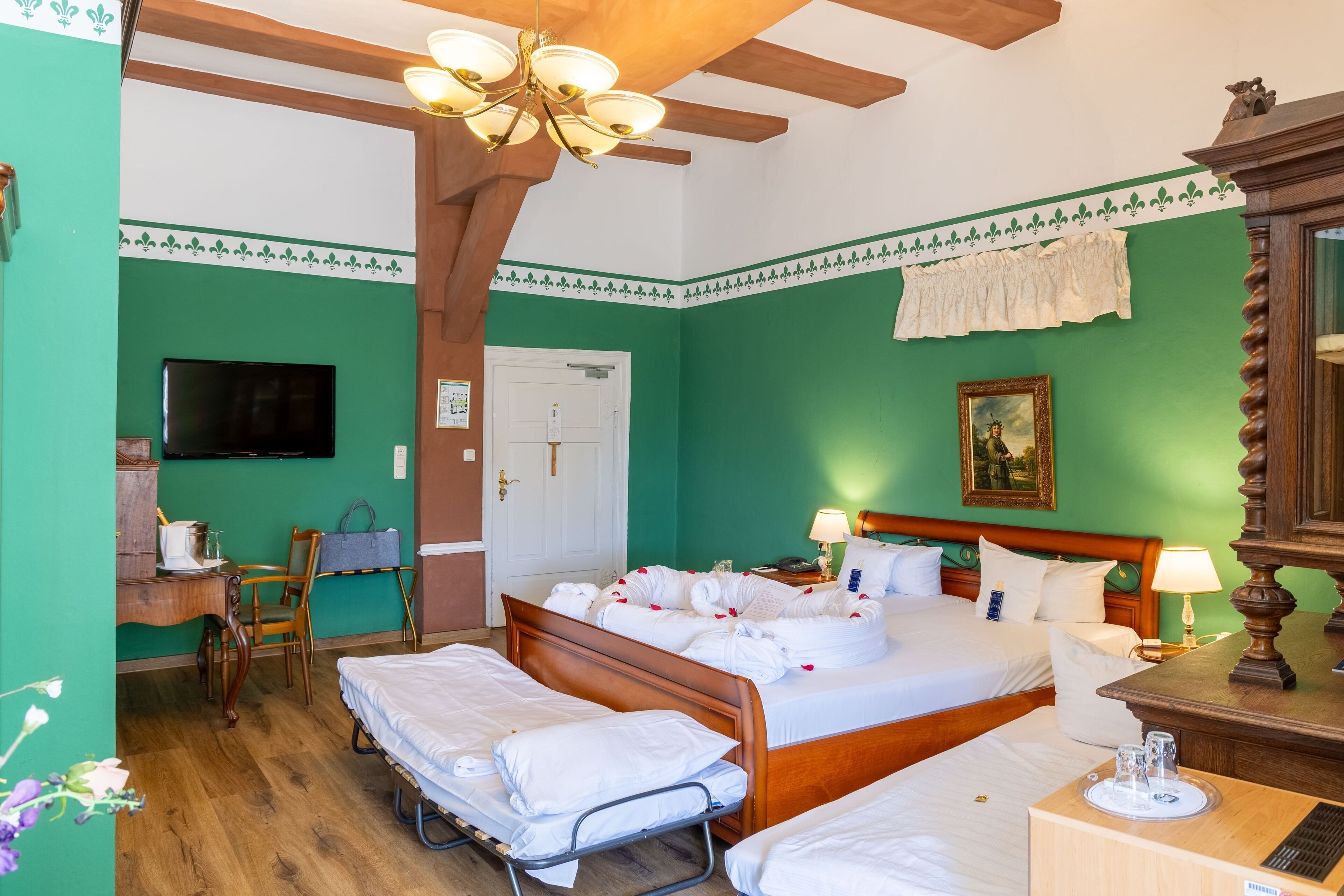 Quarto de hotel com duas camas, uma mesa com cadeira, televisão e teto de madeira.