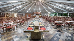 Uma ampla área de refeições interna, com teto alto e uma mesa de buffet central.