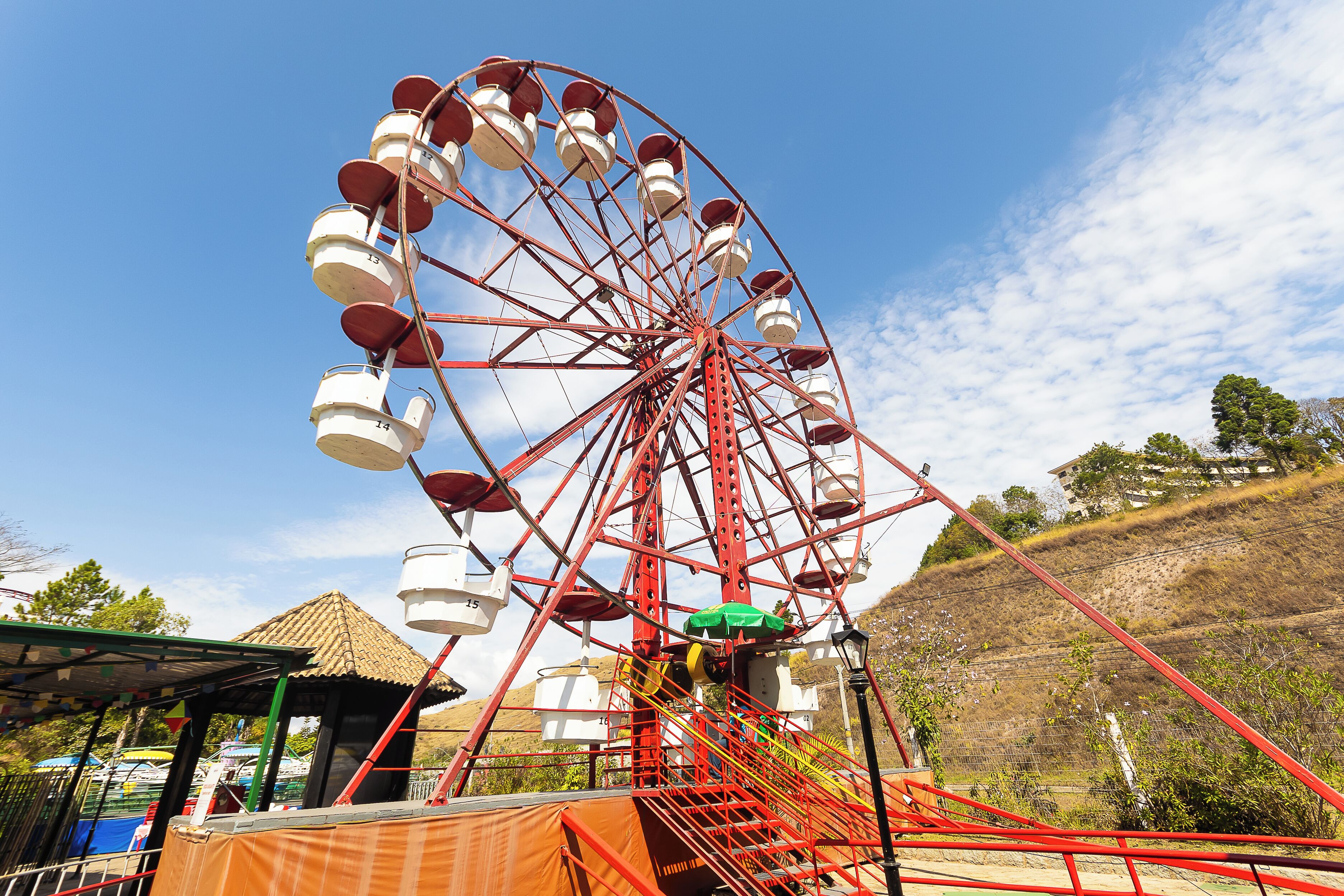 Uma grande roda gigante com cabines, uma estrutura coberta e uma colina ao fundo.